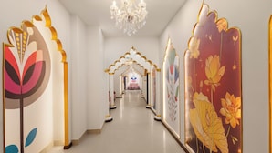 Um corredor com lustre, arcos decorativos e arte floral nas paredes.