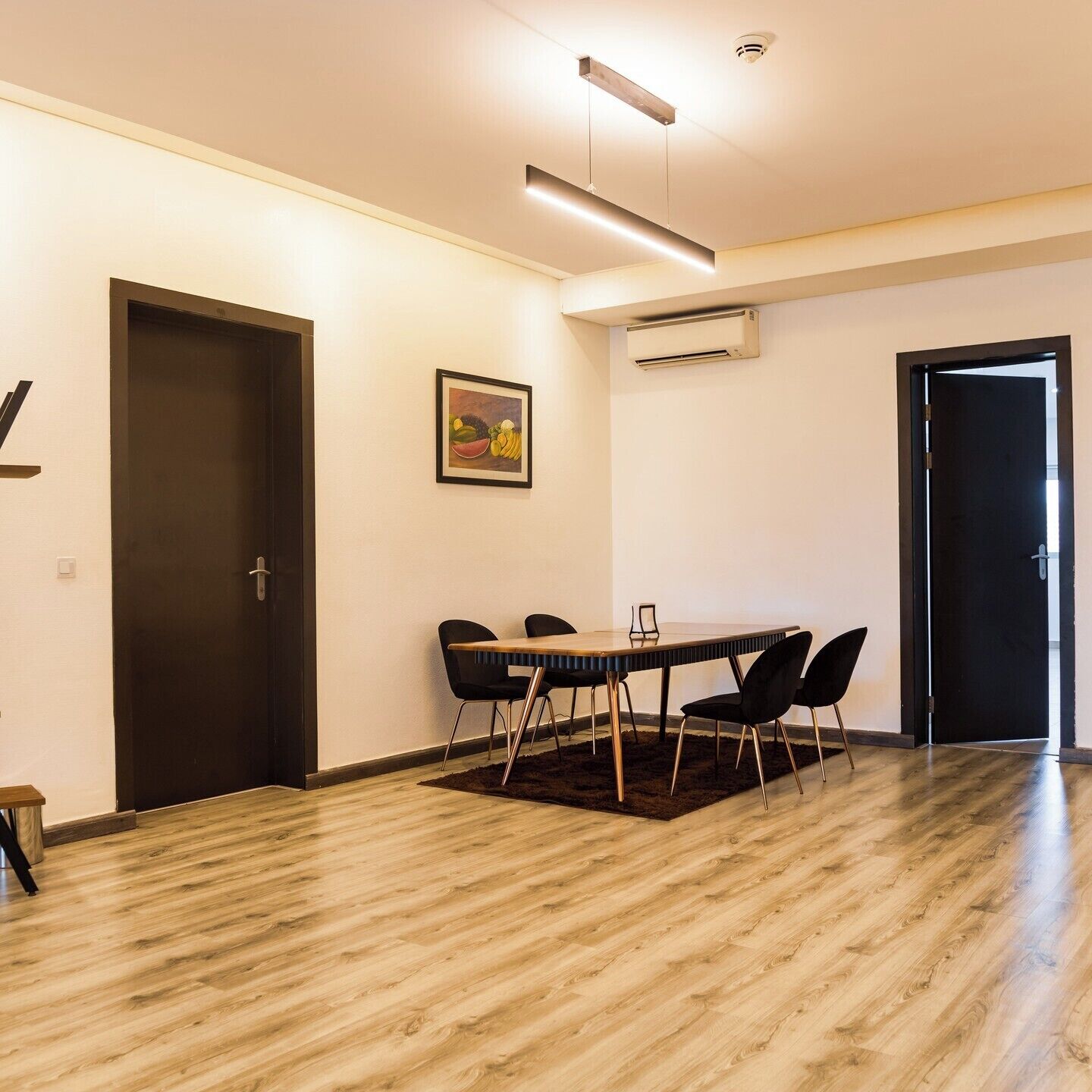 Uma sala de jantar moderna com mesa e cadeiras de madeira, um quadro na parede e um aparelho de ar condicionado.