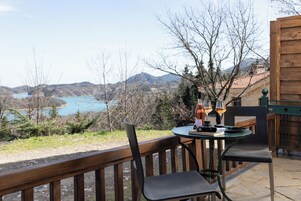 Um deck de madeira com mesa e cadeiras com vista para um lago e montanhas.