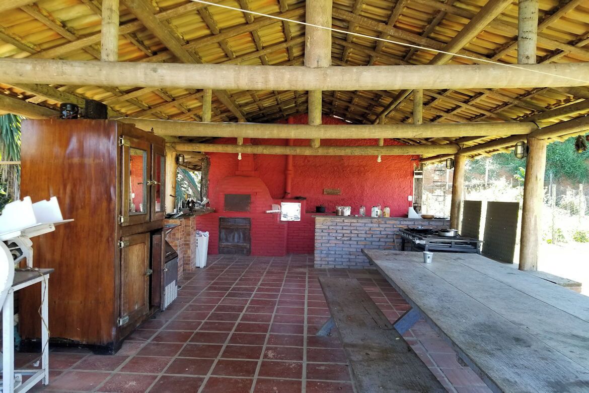 Uma área de cozinha ao ar livre coberta, com bancada de tijolo, churrasqueira e armário de madeira.
