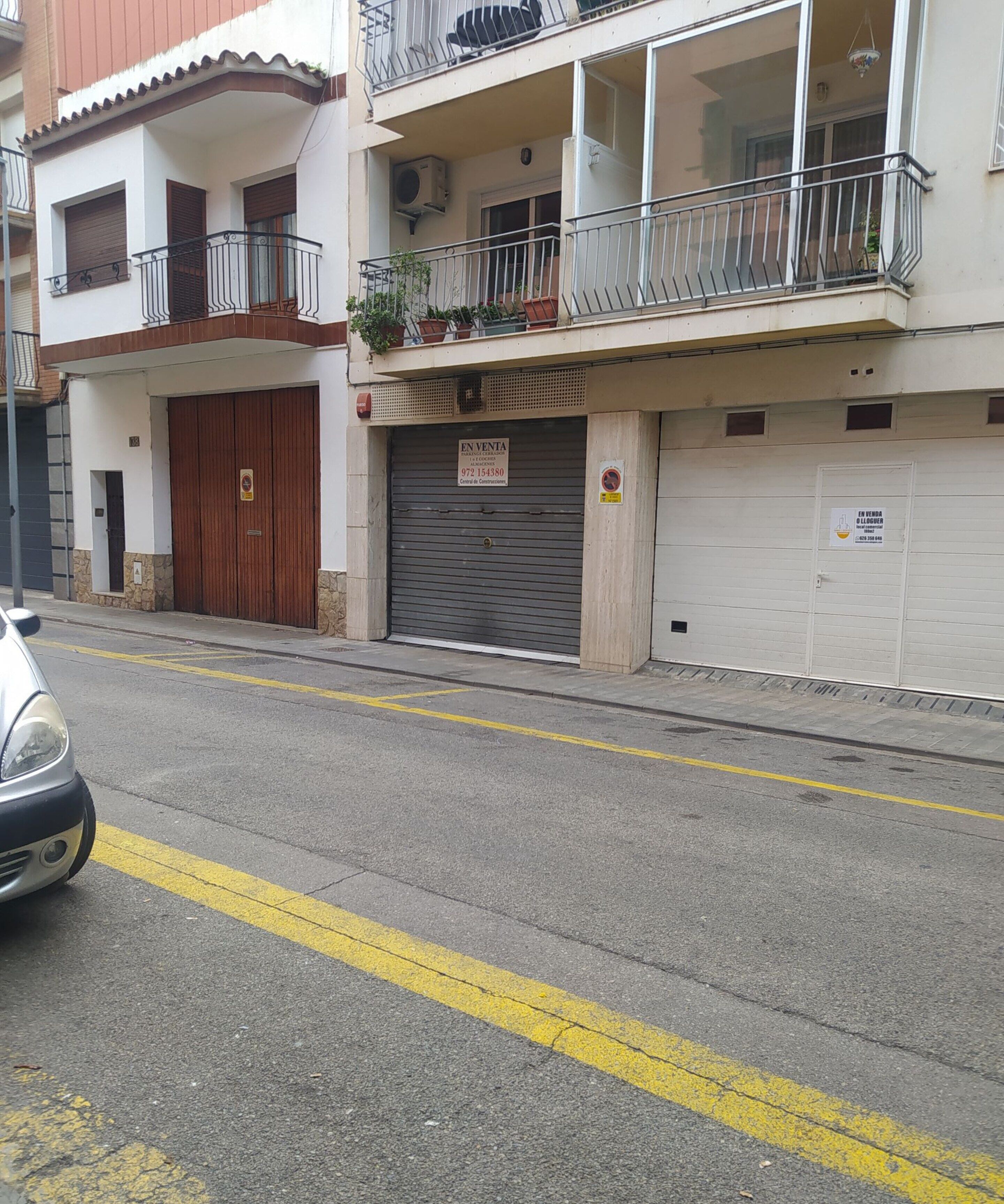 Um edifício de vários andares com uma porta de garagem fechada, varandas com grades de metal e plantas em vasos no segundo andar.