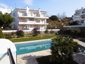 Um edifício com vários andares, varandas, piscina e jardins ajardinados.