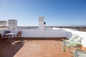 Um terraço no telhado com mesa e cadeiras, uma chaminé e vista para a paisagem.