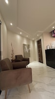 Um lobby moderno com balcão de recepção, dois sofás, uma planta decorativa e piso de mármore.