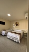 Quarto de hotel com duas camas, mesa de cabeceira, ar condicionado fixado na parede e iluminação no teto.