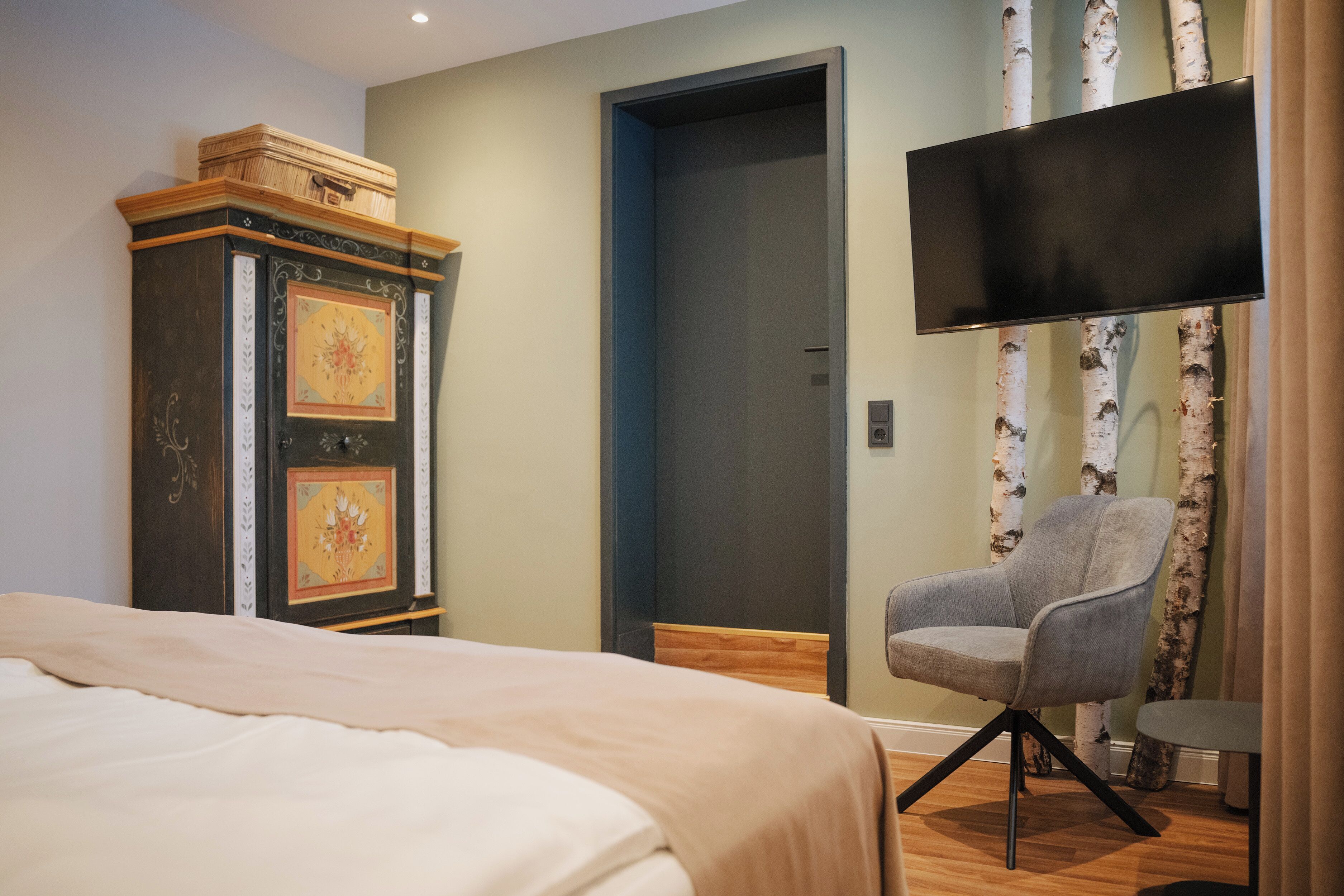 Quarto com cama, cômoda, cadeira, televisão e porta.