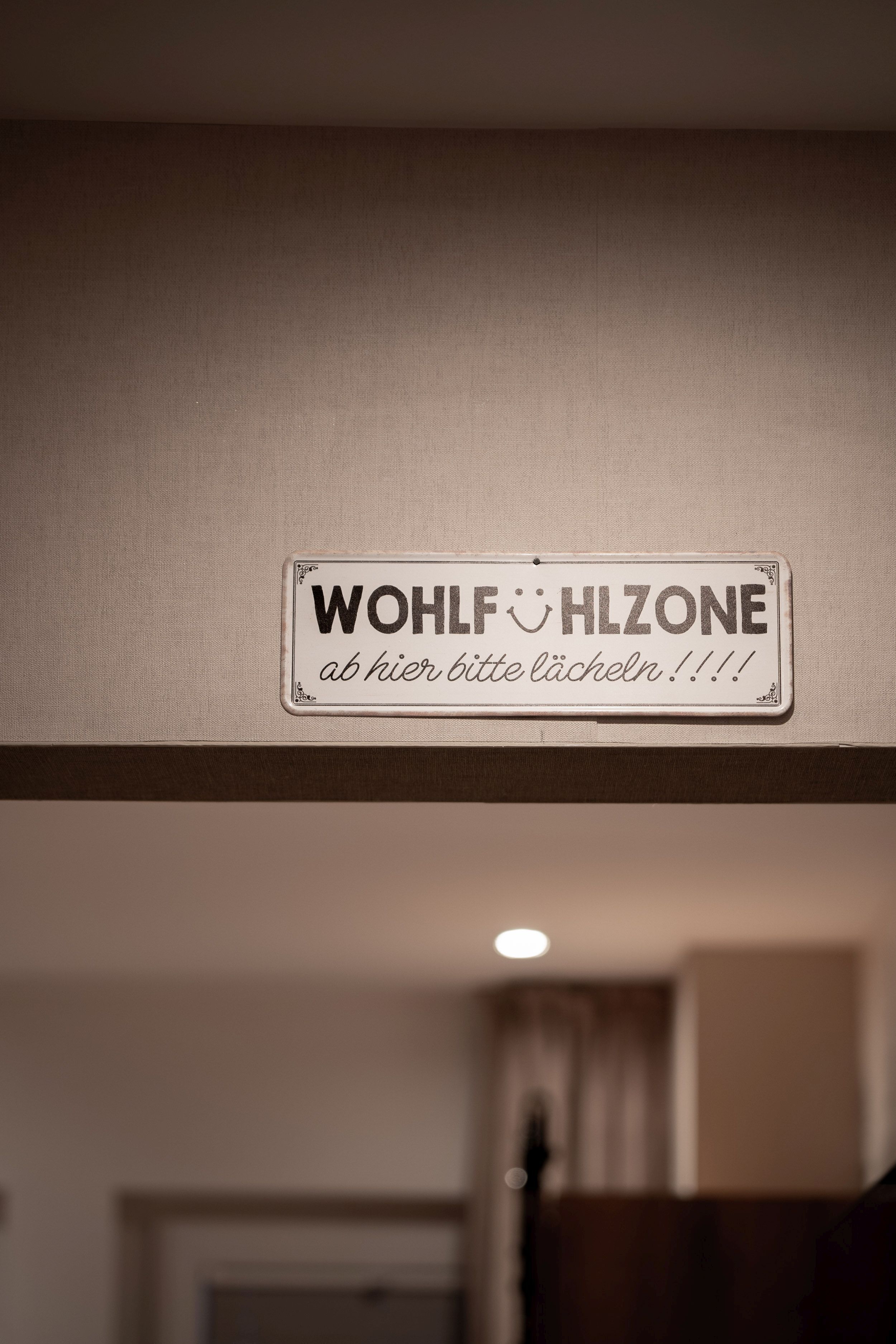 Um letreiro na parede com a mensagem 'WOHLFÖHLZONE ab hier bitte lächeln!!!'.