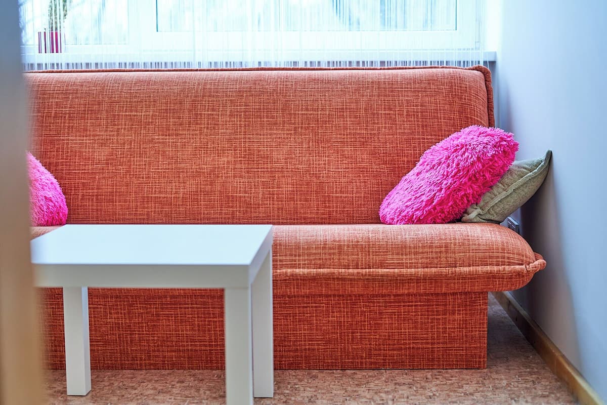 Um quarto com um sofá vermelho, uma mesa branca e um travesseiro rosa e fofo.