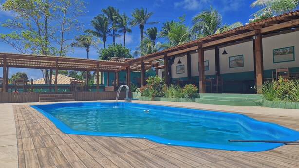 Piscina com deck de madeira, cercada por um alpendre coberto com vigas de madeira e telhado de azulejo.