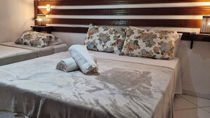 Quarto de hotel com duas camas, cada uma com toalha dobrada e almofadas estampadas com flores.