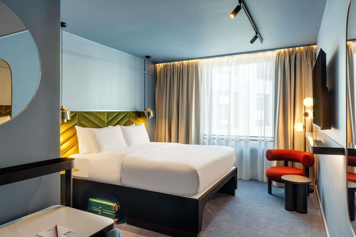 Quarto de hotel com cama, mesa de cabeceira, cadeira e espelho.