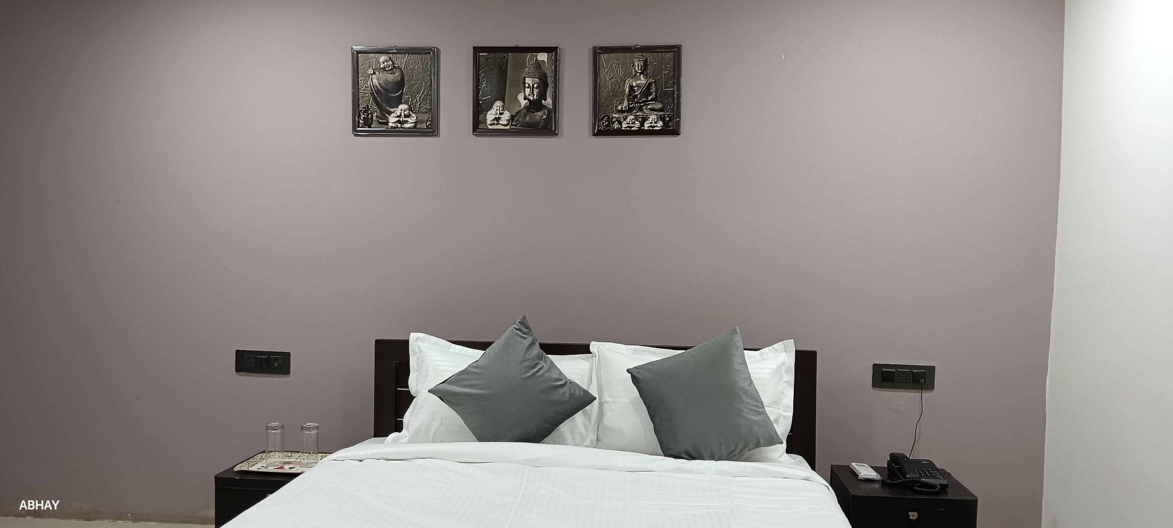 Quarto com cama, duas almofadas, mesa de cabeceira com telefone e três quadros na parede.