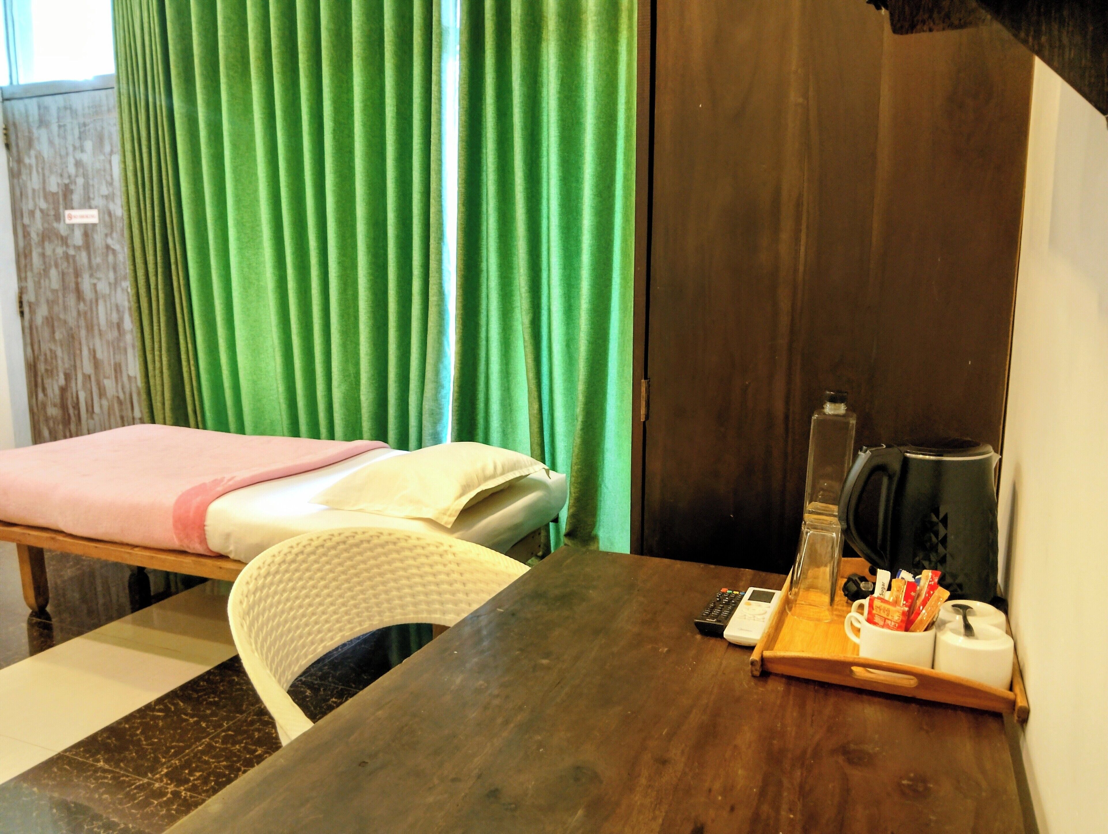 Quarto de hotel com cama, mesa de madeira, cadeira, cafeteira e bandeja com chávenas e snacks.