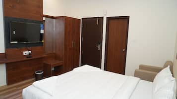 Quarto com cama, televisão fixada numa parede de madeira, guarda-roupa e uma porta.