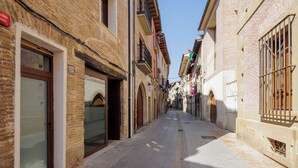Uma rua estreita ladeada por edifícios tradicionais, com janelas e portas em arco, e um céu claro acima.