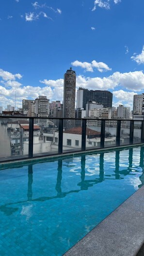 Piscina no terraço com vista para o horizonte urbano, incluindo edifícios altos e um céu azul límpido.