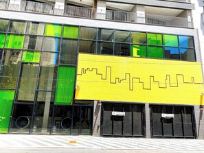 Um edifício moderno com grandes janelas, uma placa amarela com um gráfico de linhas e uma indicação de entrada e saída.