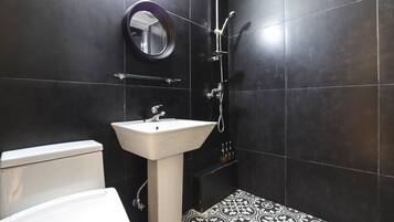 Um banheiro moderno com pia branca, espelho redondo, chuveiro manual e azulejos com padrão preto.