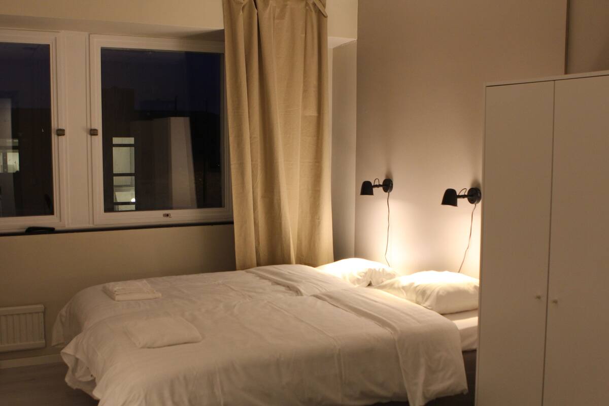 Quarto com cama, janela com cortinas, guarda-roupa e luminária na parede.