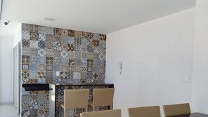 Uma sala de jantar com mesa preta e cadeiras de vime, painel de fundo estampado e parede branca.