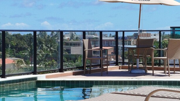 Área de piscina no terraço com vista para a cidade, uma mesa com cadeiras e um guarda-sol.