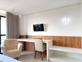 Espaço de escritório moderno com escrivaninha, duas cadeiras, TV fixada na parede e vista para o exterior.