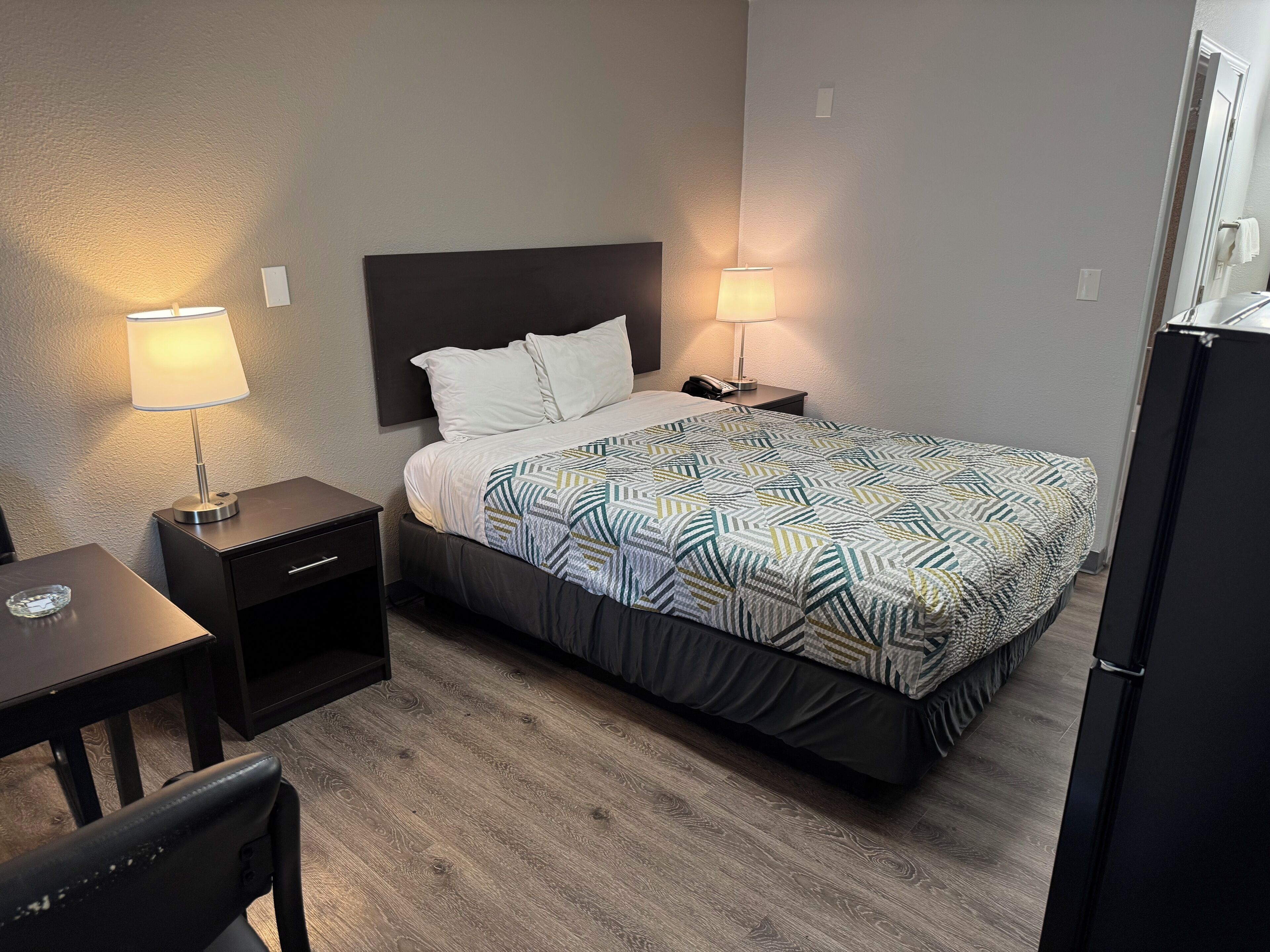 Quarto de hotel com cama, duas mesas de cabeceira, escrivaninha, cadeira e um refrigerador.