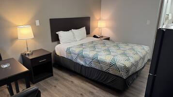 Quarto de hotel com cama, duas mesas de cabeceira, escrivaninha, cadeira e um refrigerador.