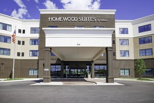 Entrada de hotel com placa 'Homewood Suites by Hilton', uma bandeira e céu claro.