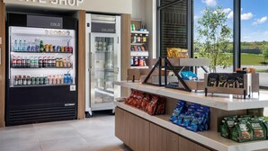 Loja de suítes de hotel com dispensadores de bebidas refrigeradas e geladas, pacotes de lanches e bebidas, e vista para o exterior.