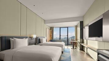 Quarto de hotel com duas camas, televisão, uma mesinha e vista para a cidade.