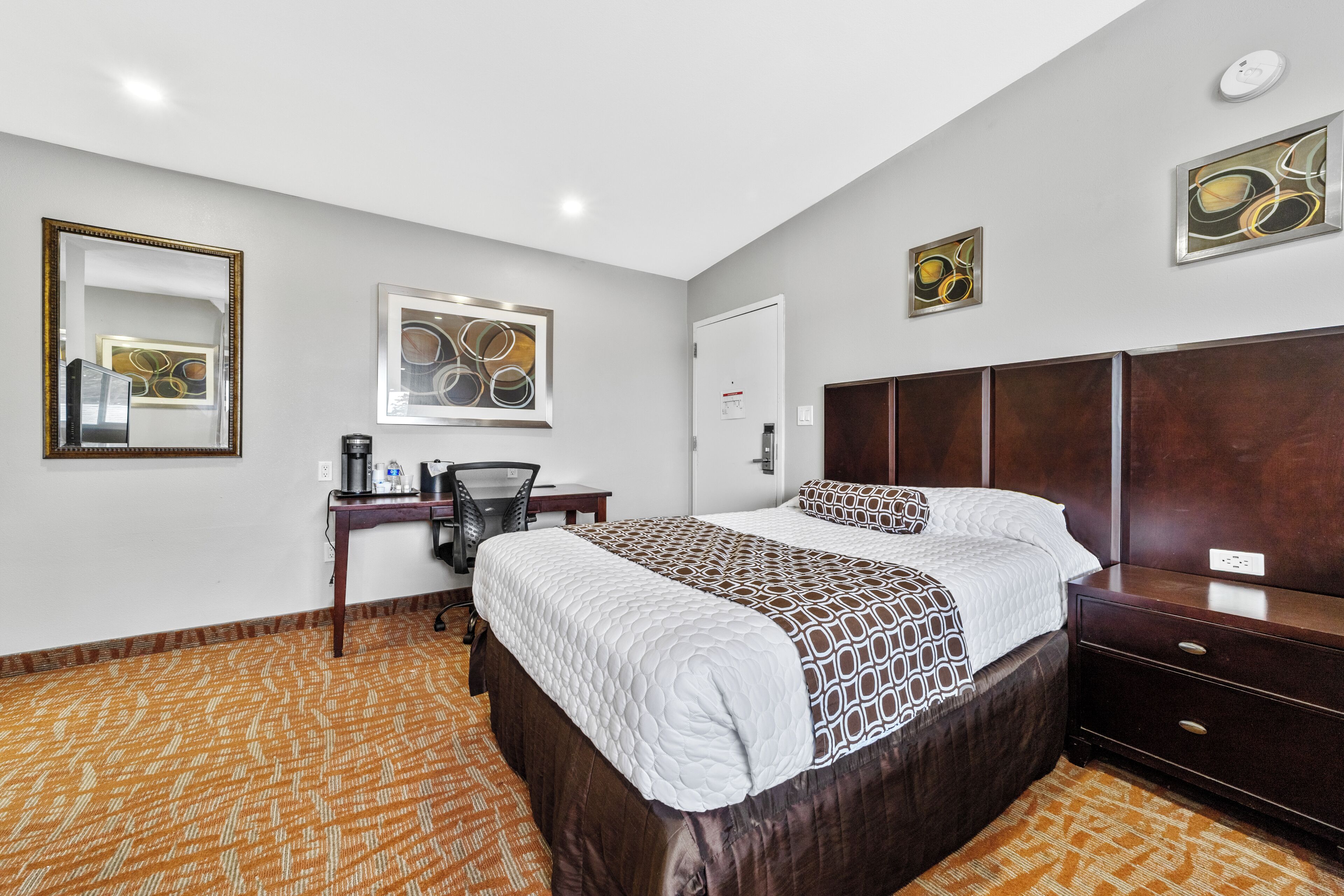 Quarto de hotel com uma cama grande, uma mesa com cadeira, uma cafeteira e obras de arte nas paredes.