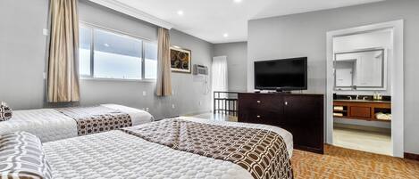 Quarto de hotel com duas camas, uma televisão, cômoda e banheiro visível por uma porta aberta.