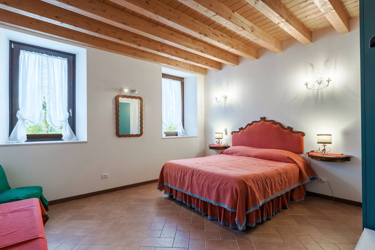 Quarto com uma cama grande, duas janelas com cortinas, teto de madeira e iluminação embutida na parede.