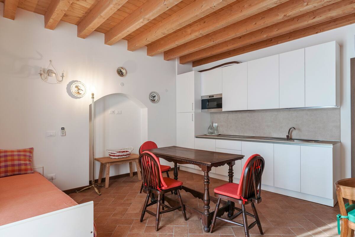 Uma cozinha compacta com armários brancos, uma mesa de jantar de madeira e cadeiras vermelhas.