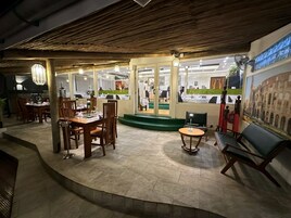 Um restaurante com teto de madeira, mesas com cadeiras e um espaço coberto por carpete verde.
