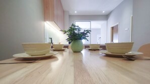 Uma mesa de jantar com quatro tigelas e pires, um vaso de planta, e um interior moderno com teto de madeira e uma janela.