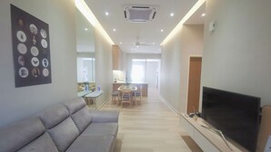 Uma sala de estar moderna com um sofá cinzento, uma televisão de tela plana e uma área de jantar com mesa e cadeiras.