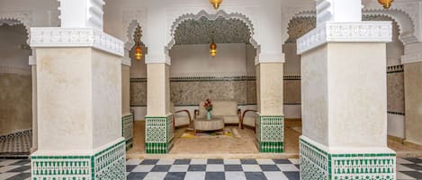 Um interior com piso xadrez, um sofá e colunas estampadas.