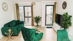 Uma sala de estar com um sofá verde, uma mesa de centro de vidro e uma televisão.