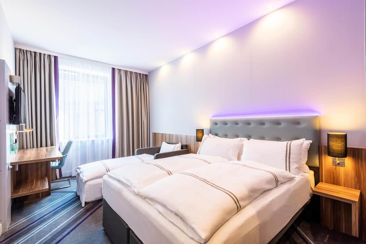 Quarto de hotel com uma cama grande, uma escrivaninha, uma cadeira e uma televisão.