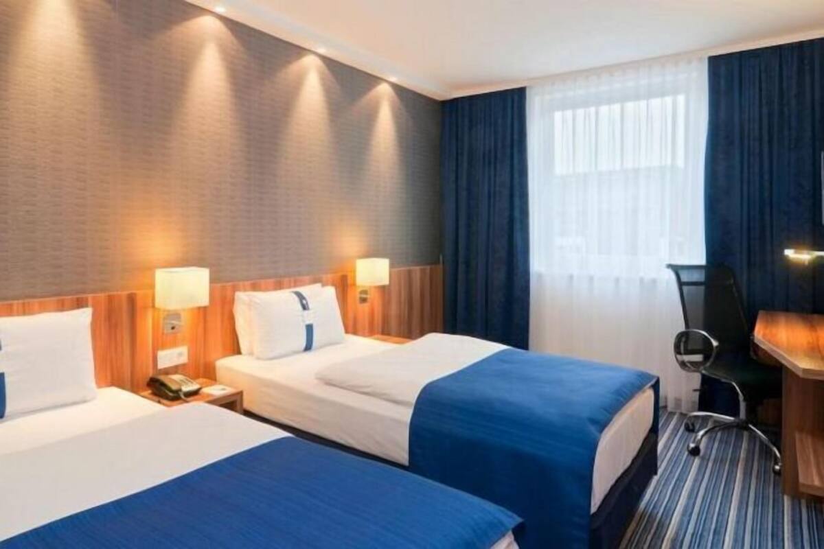 Quarto de hotel com duas camas, uma escrivaninha e uma cadeira.