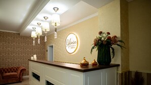 Uma área de recepção com um balcão branco, uma placa na parede e um vaso de flores.