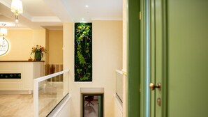 Um hall de hotel com uma escadaria de mármore, uma porta verde e um objeto decorativo fixado na parede.