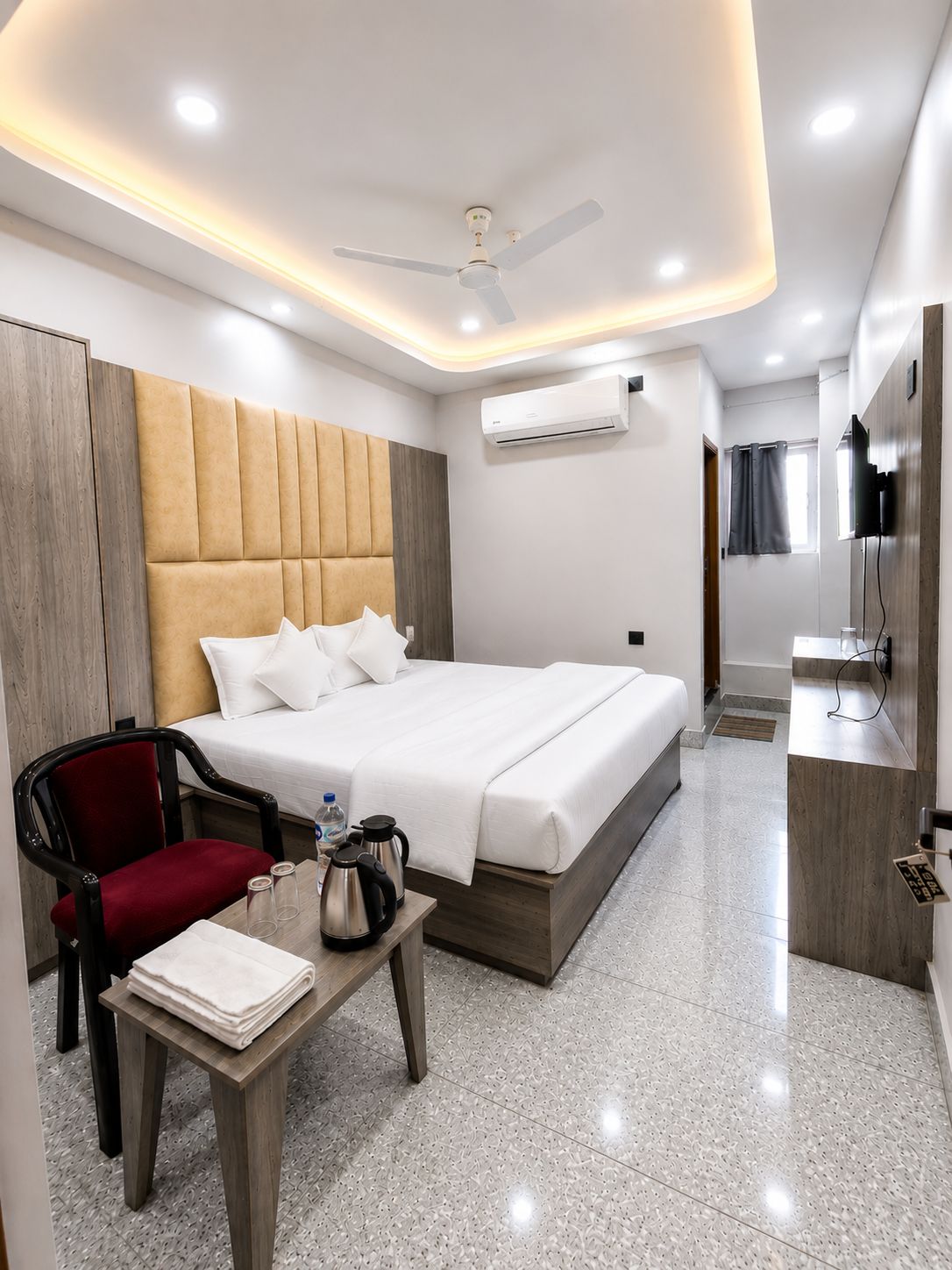 Quarto de hotel moderno com cama, escrivaninha com chaleira, cadeira e televisão.