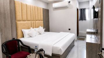 Quarto de hotel moderno com cama, escrivaninha com chaleira, cadeira e televisão.
