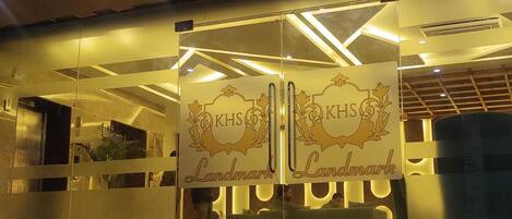 Entrada de hotel com fachada de vidro e o nome "KHS Landmark" em destaque.