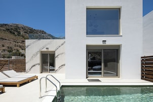 Um edifício moderno com piscina, deck de madeira e uma montanha ao fundo.