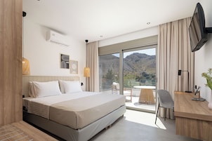 Quarto de hotel moderno com uma cama grande, uma escrivaninha, televisão de tela plana e varanda com vista para as montanhas.
