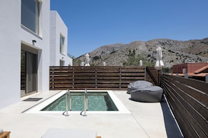 Uma área de piscina moderna ao ar livre, com cerca de madeira, um edifício branco e montanhas ao fundo.
